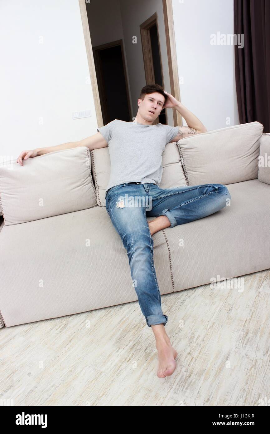Handsome young man holding remote control and looking bored while ...