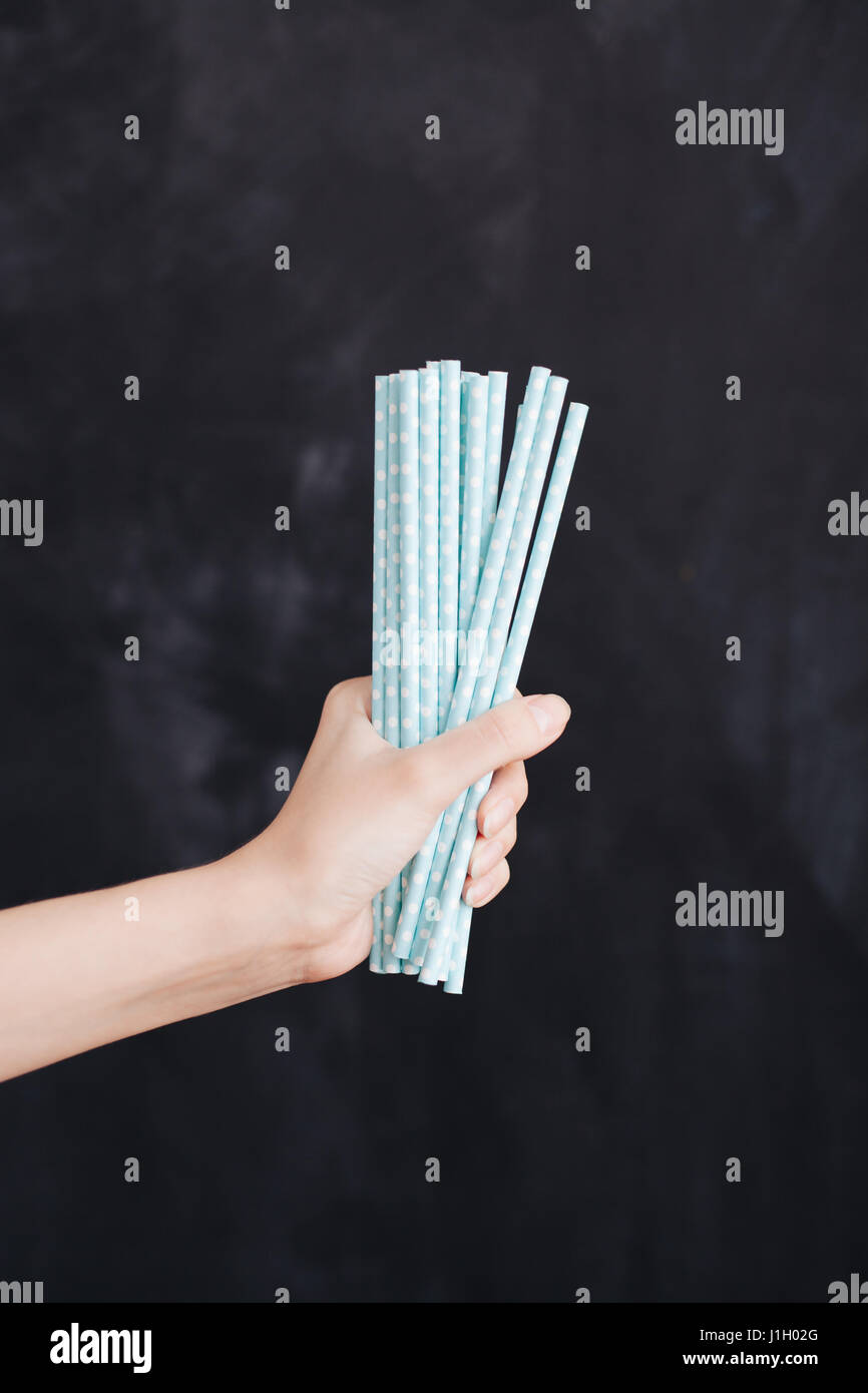 Woman hand hold cocktail straw blue on black background Stock Photo - Alamy