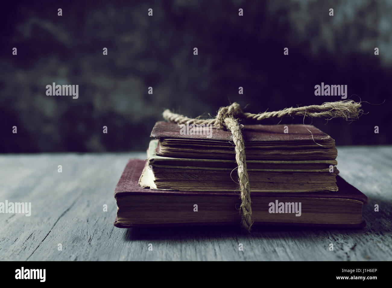 a pile of old books tied with a jute string on a rustic wooden table ...