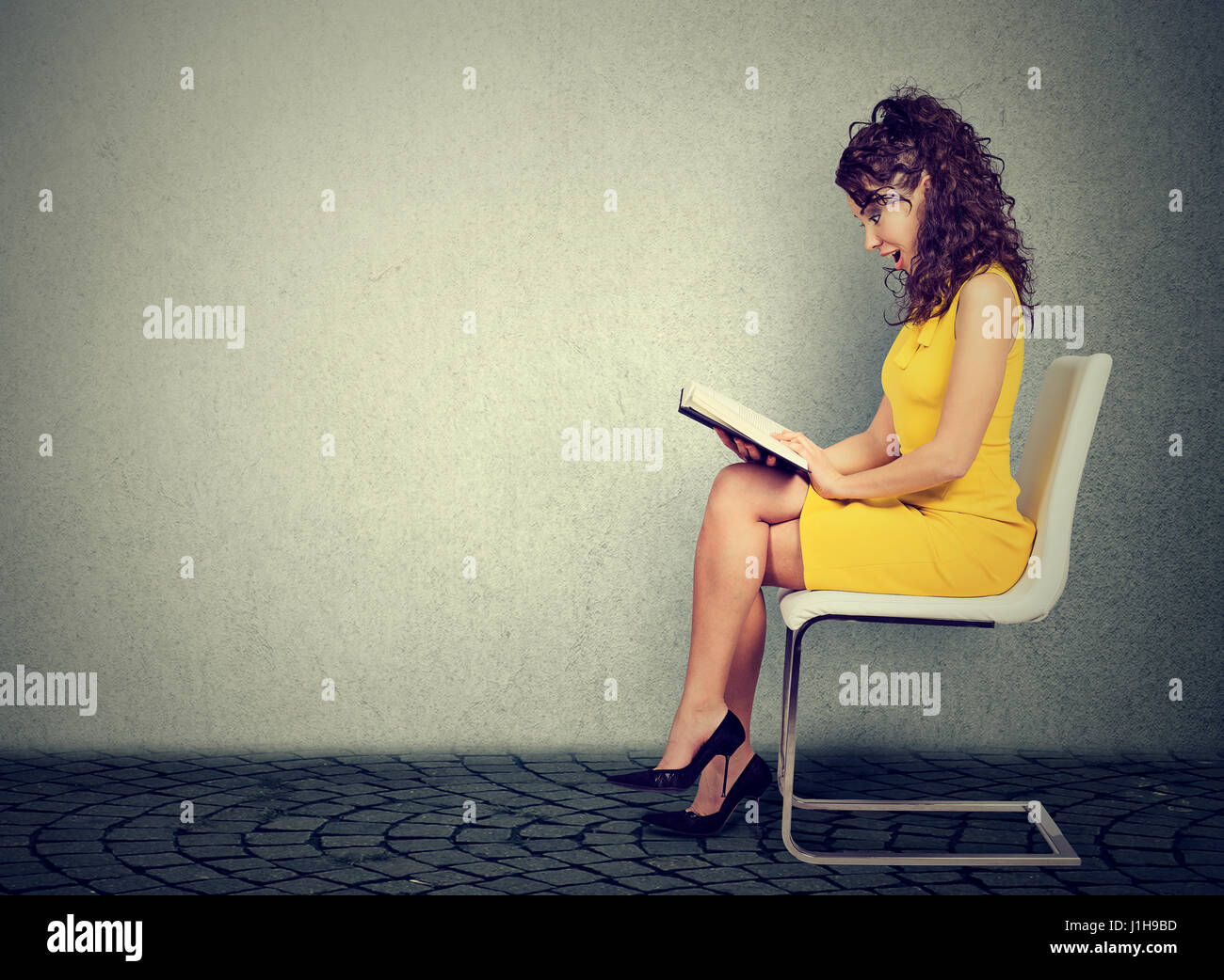 Side profile of a young woman reading a book sitting on a chair Stock ...