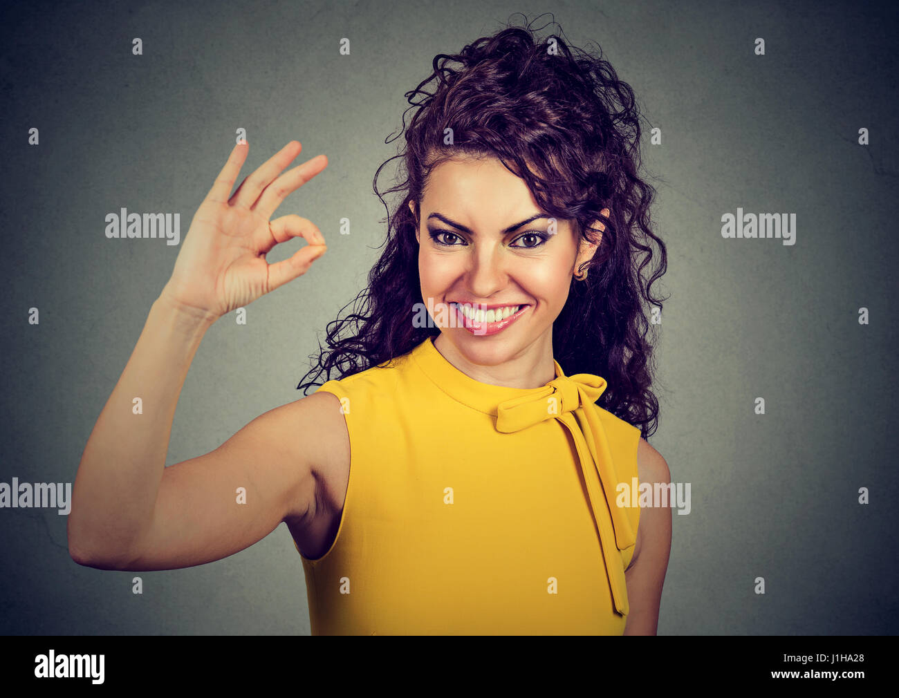 Laughing woman in yellow dress showing ok sign isolated on gray ...