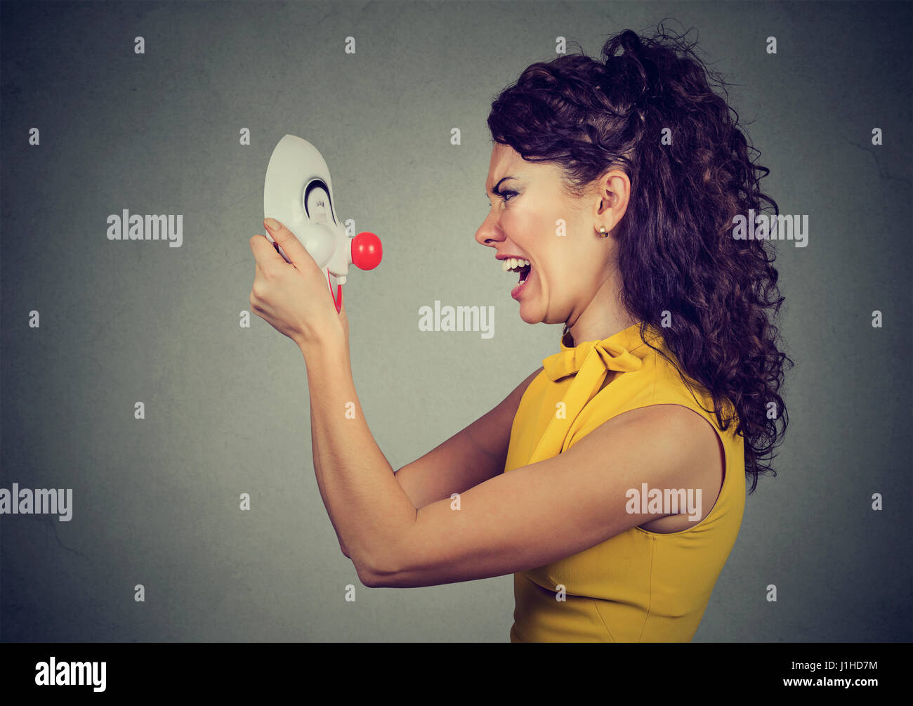 Side profile of an angry young woman screaming at happy clown mask ...
