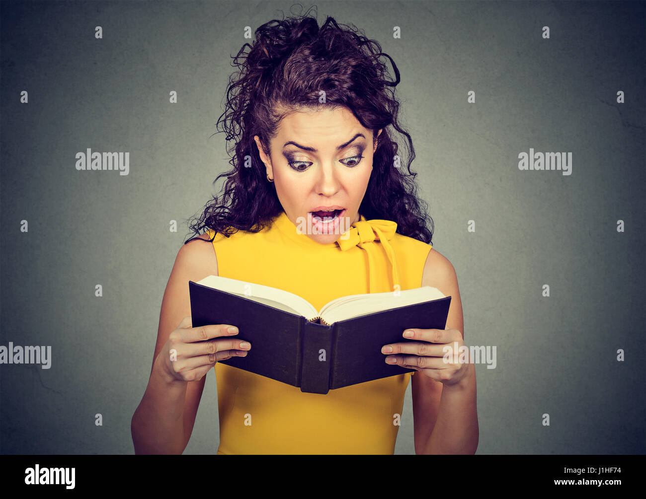 Amazed shocked woman reading a book isolated on gray wall background ...