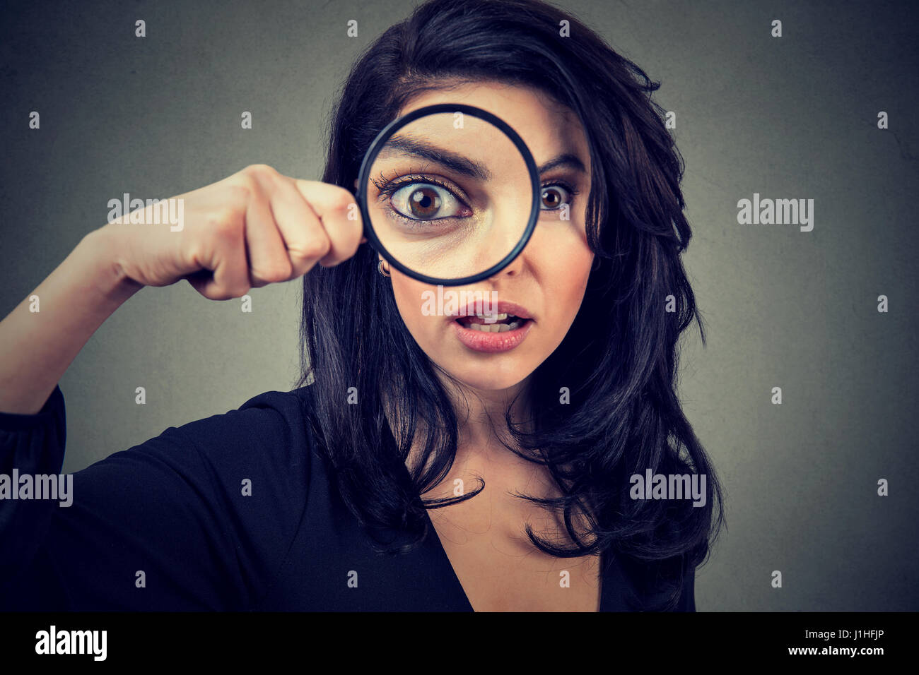 Surprised woman looking through magnifying glass isolated on gray wall ...
