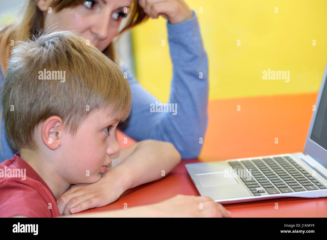 A little boy works or communicates on a laptop under the supervision of ...