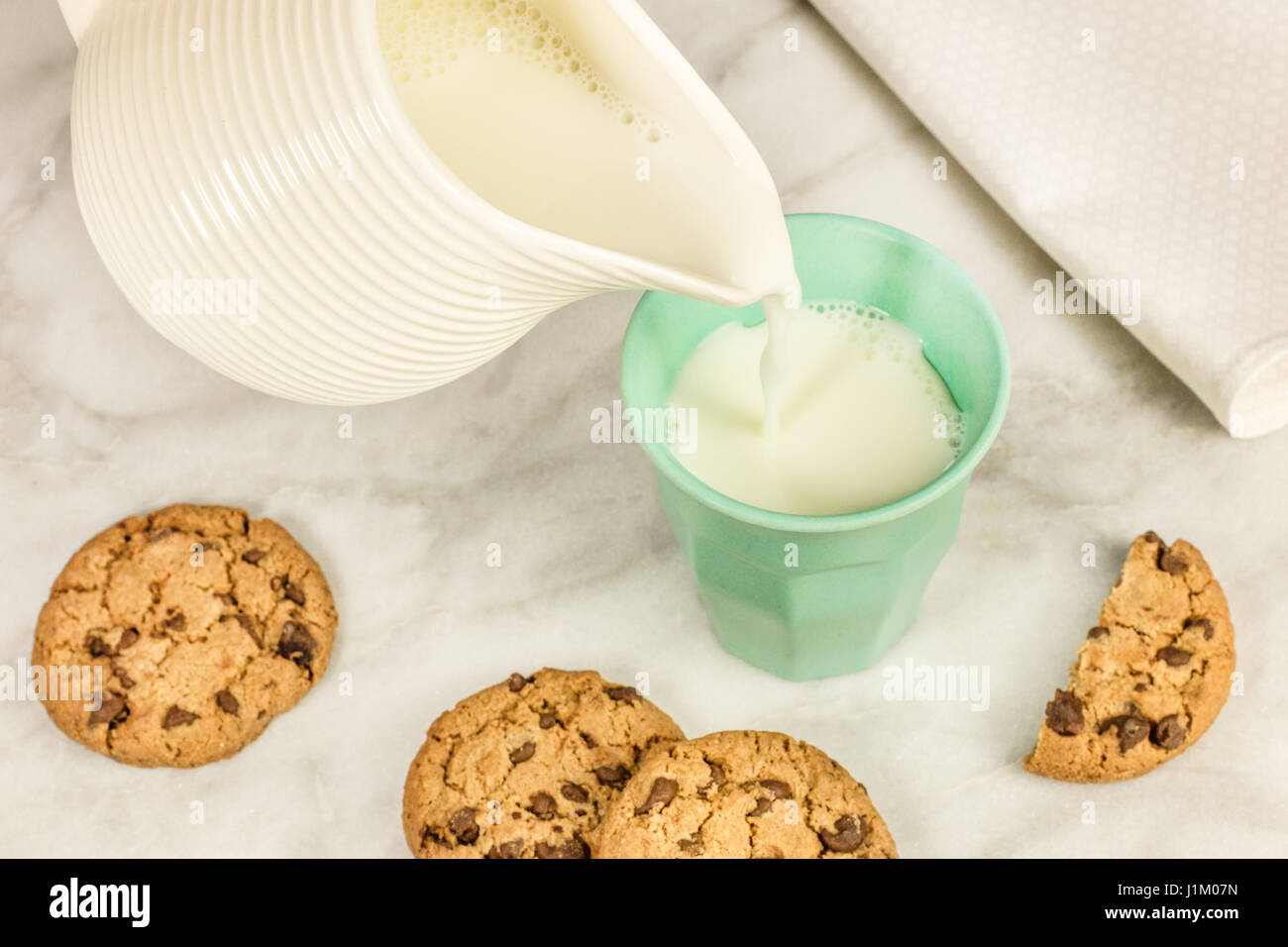 A closeup of milk poured into a glass from a jar, with chocolate chips ...