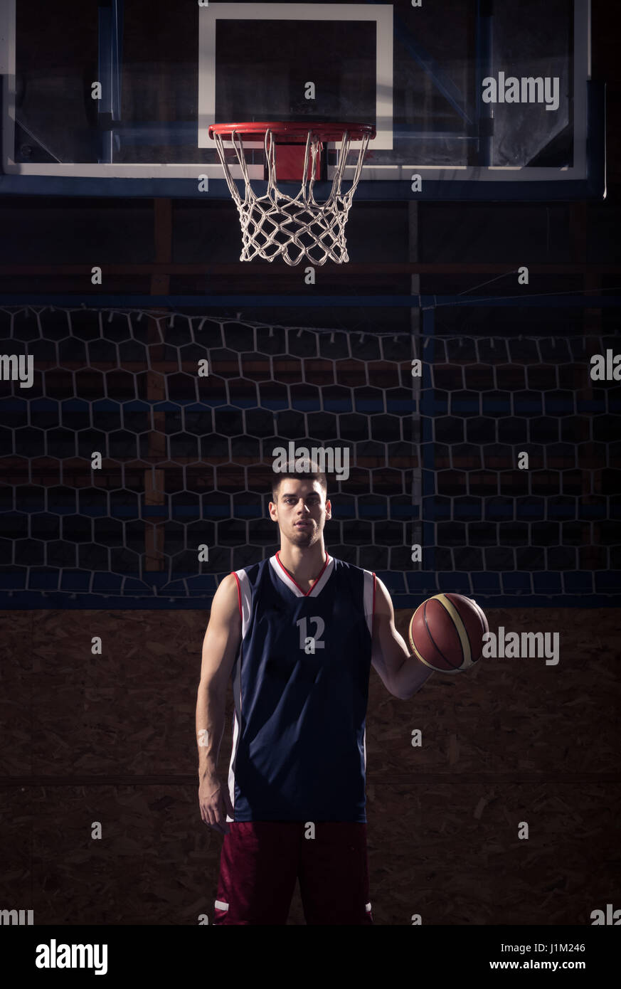 one young adult man, basketball player ball rim net, indoors dark ...