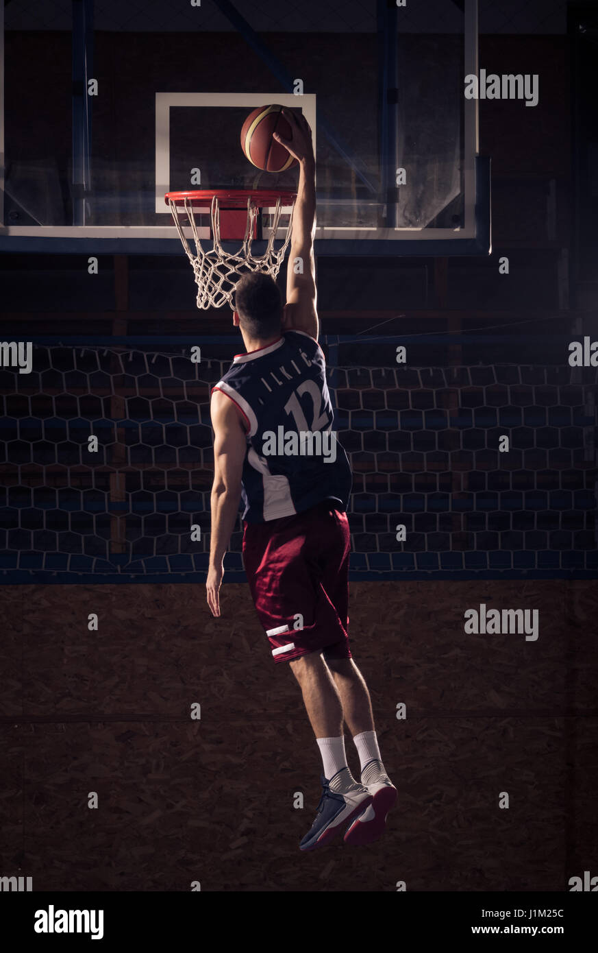 one young adult man, basketball player, one hand slam dunk, indoors ...