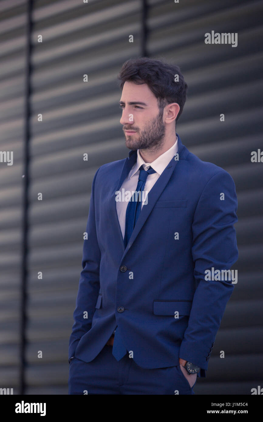 one young man standing, formal wear suit, looking sideways, outdoors ...