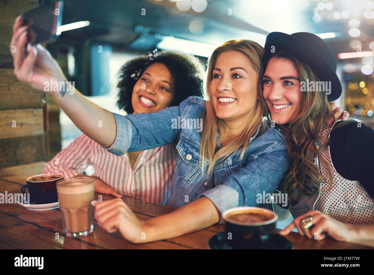 Three attractive girlfriends posing for a selfie together in a cafe as ...