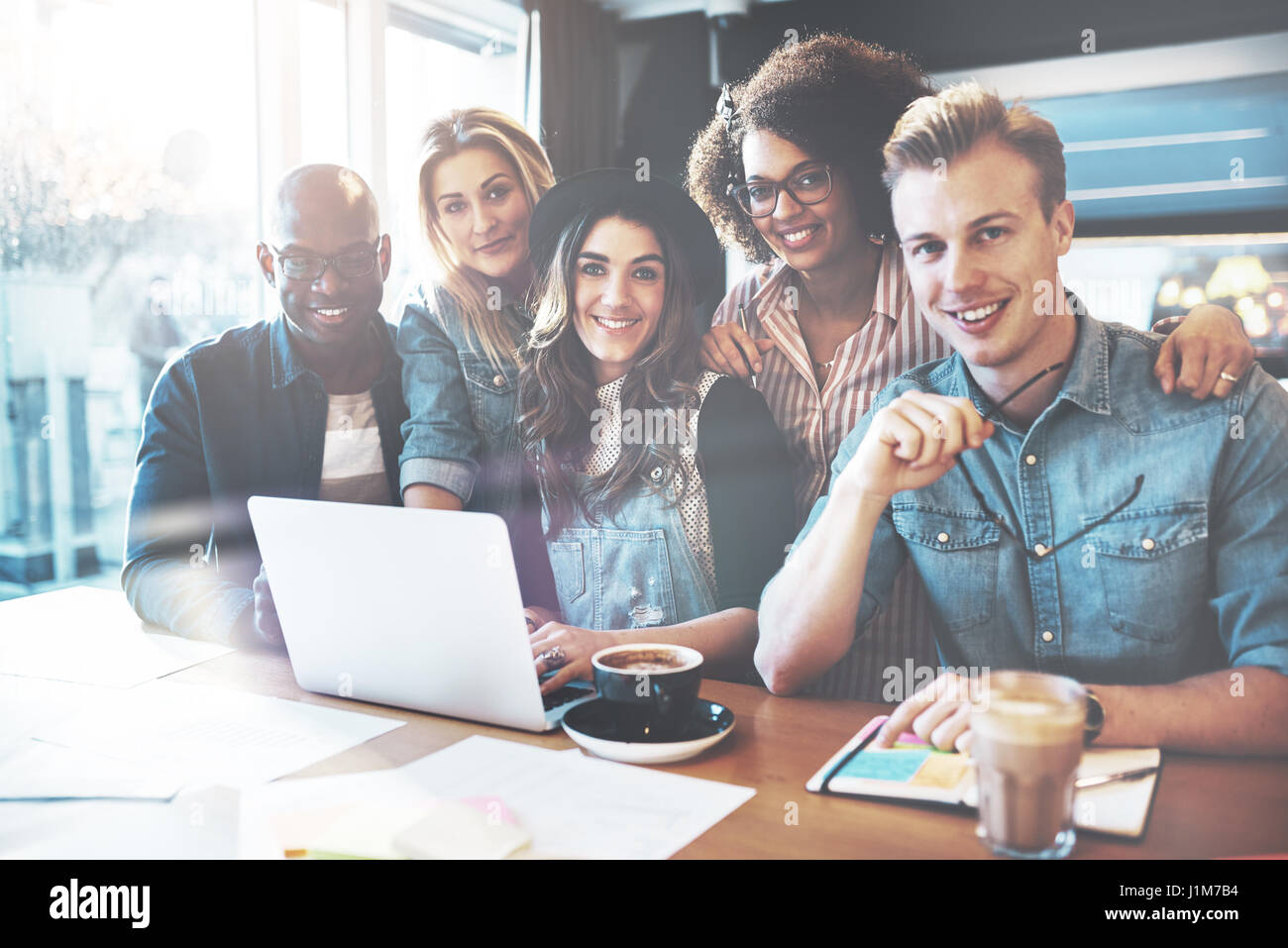 Smiling group of coworkers in small office seated around laptop ...