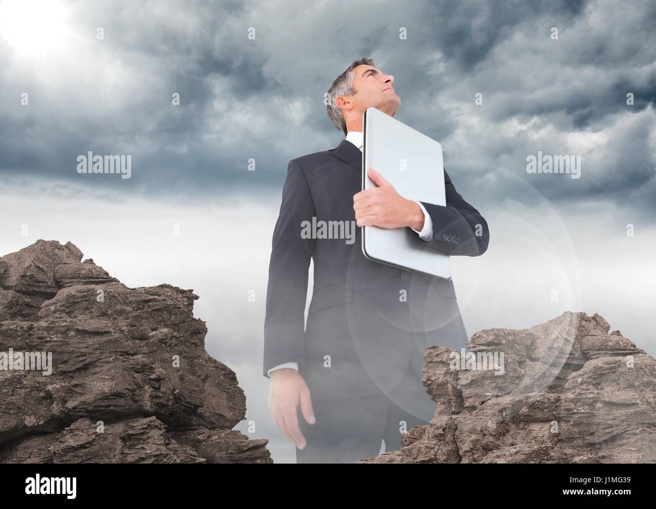 Digital composite of Business man with laptop and flare looking up ...