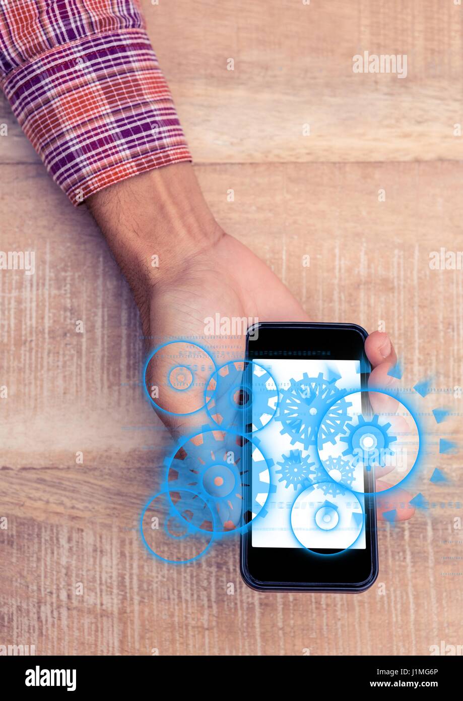Digital composite of Overhead of hand with phone showing blue cog ...