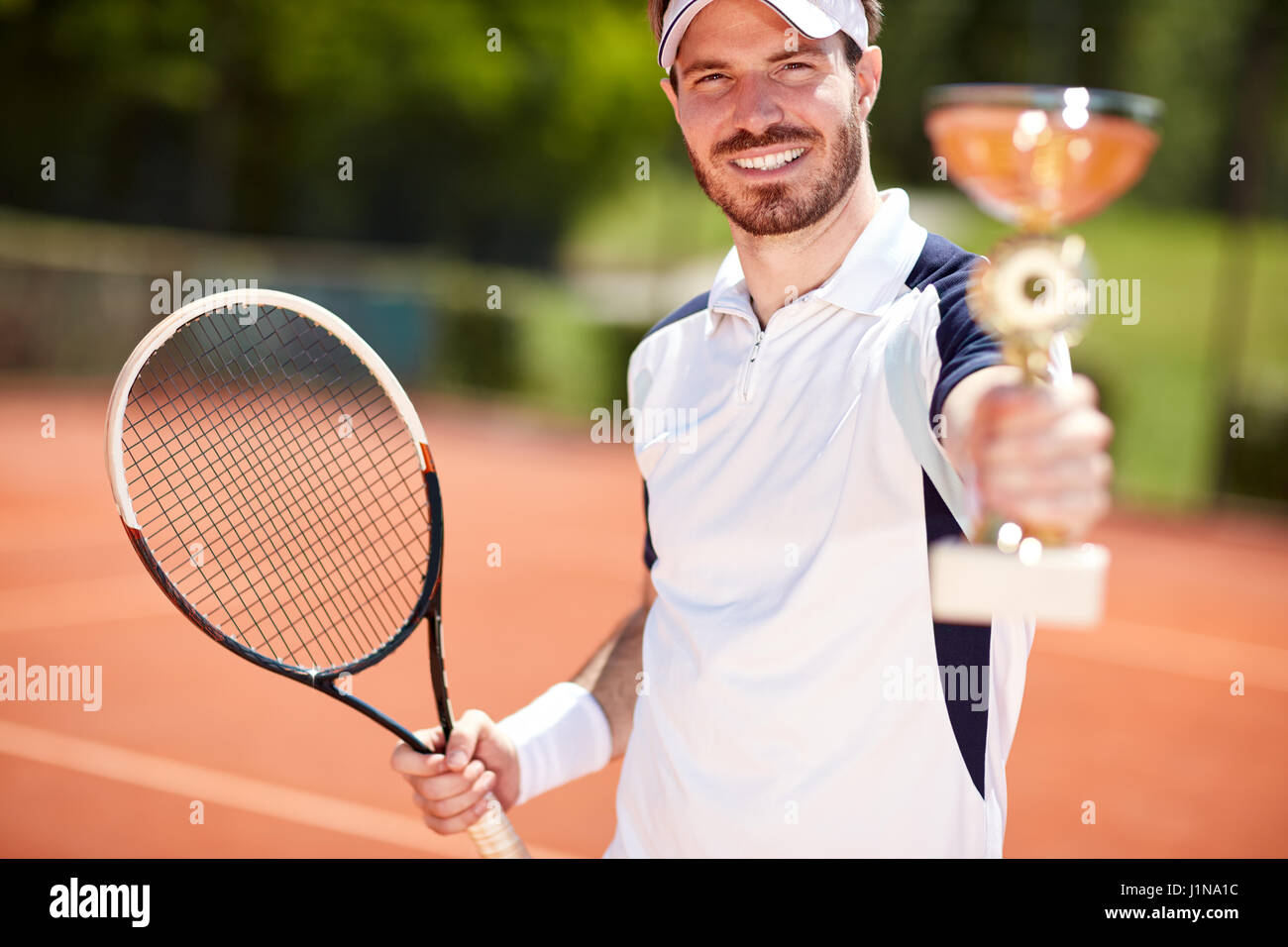 Male winner in tennis holding beaker and racket Stock Photo - Alamy