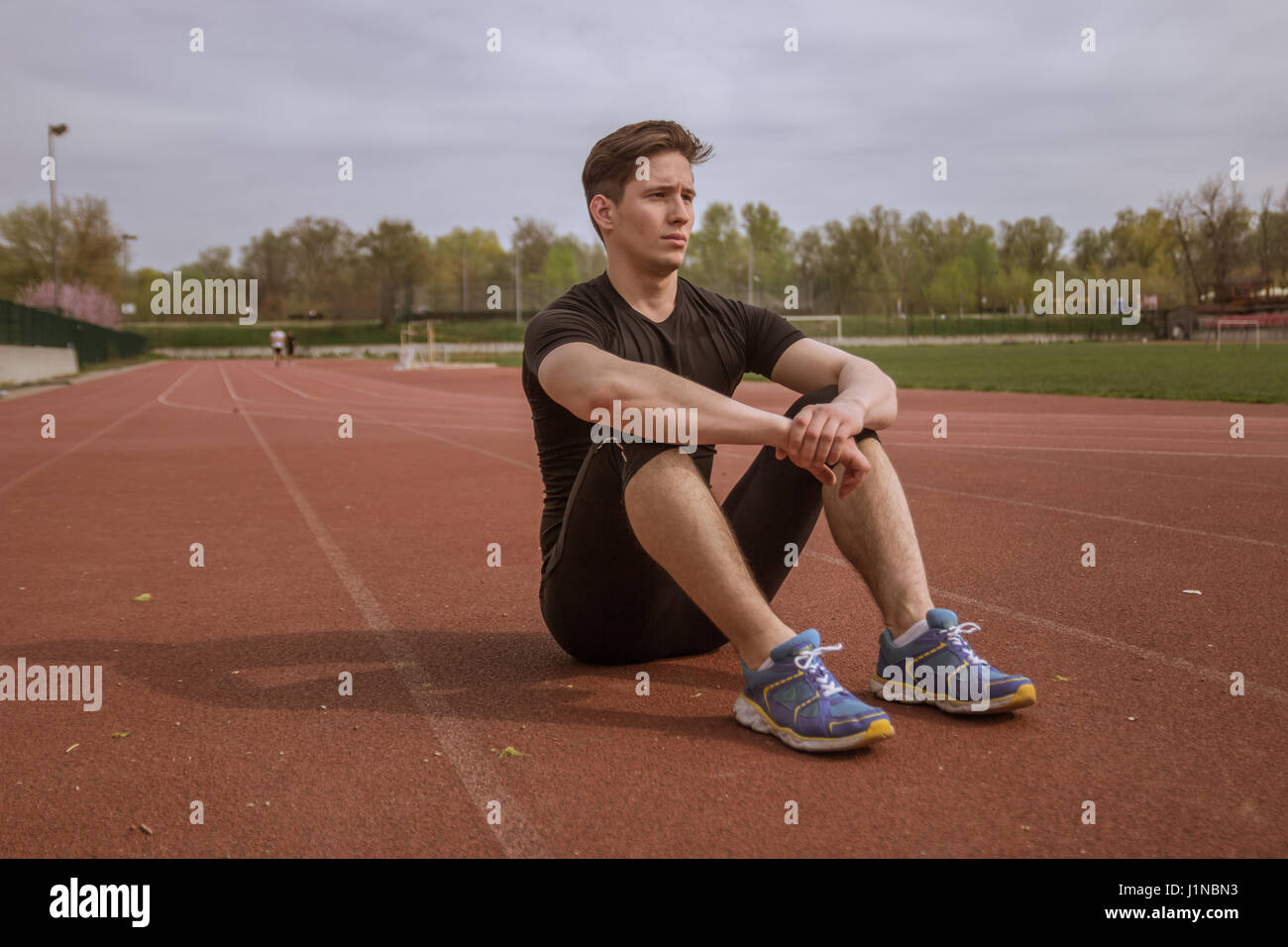one young man, relaxing sitting on red running tracks, fitness athlete ...