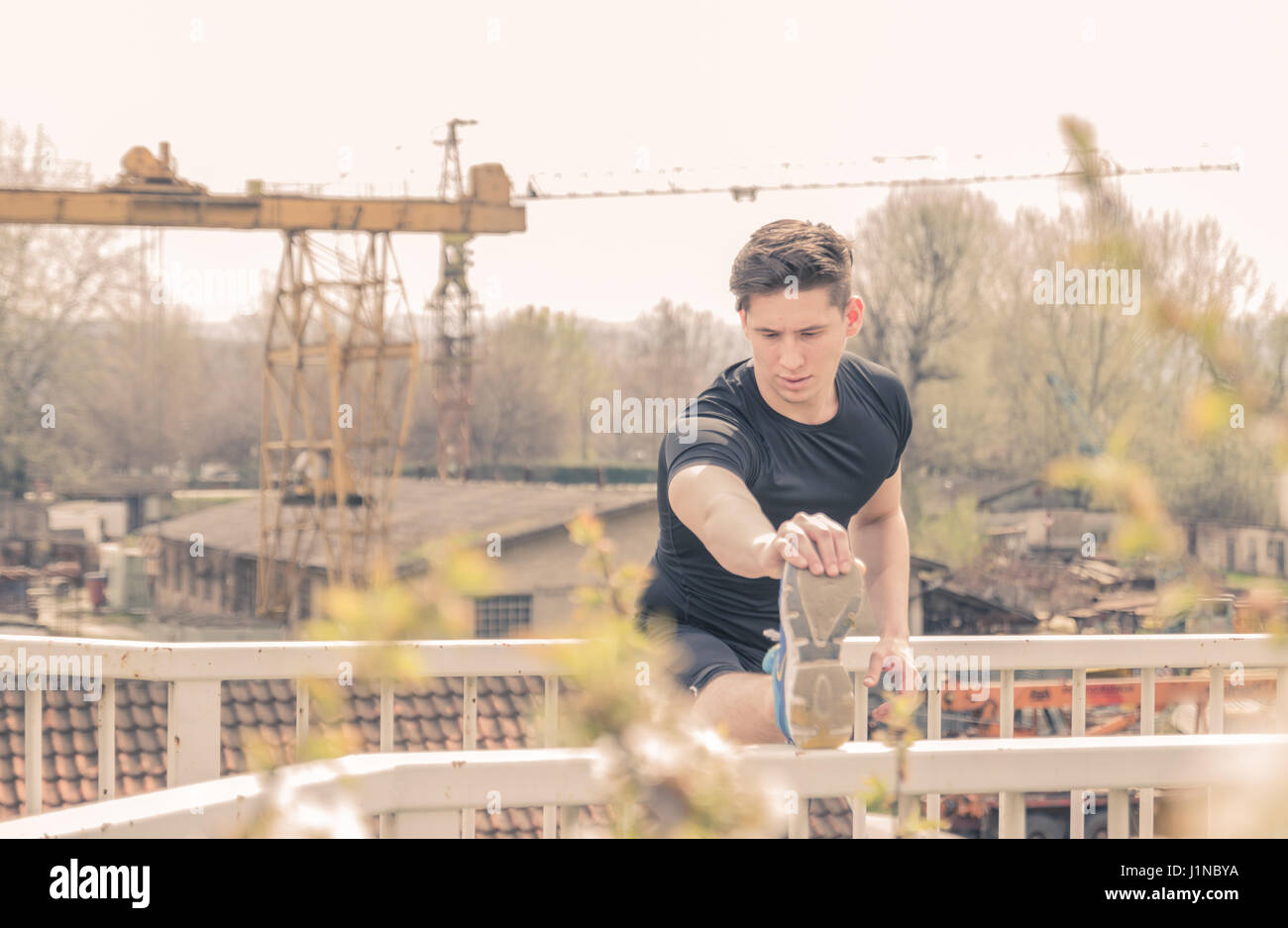 one young man, stretching leg on fence, outdoors industry tree Stock ...
