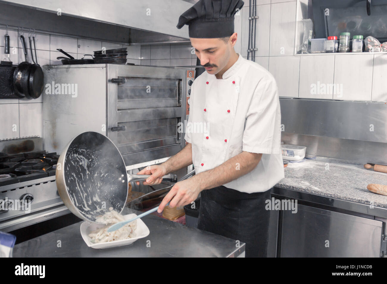 one young adult man, professional chef finishing pan parmesan pasta ...