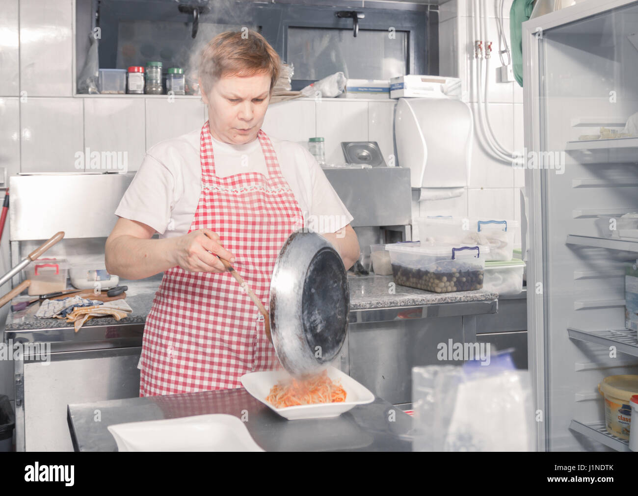 one mature woman cooking steam pan, pasta dish, commercial kitchen ...