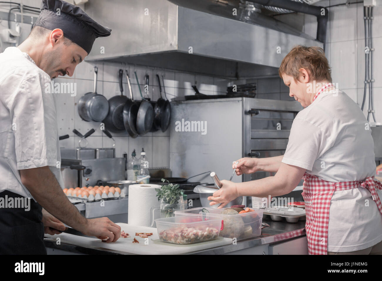 two people, chef assistant cooking food, commercial kitchen, rear view ...