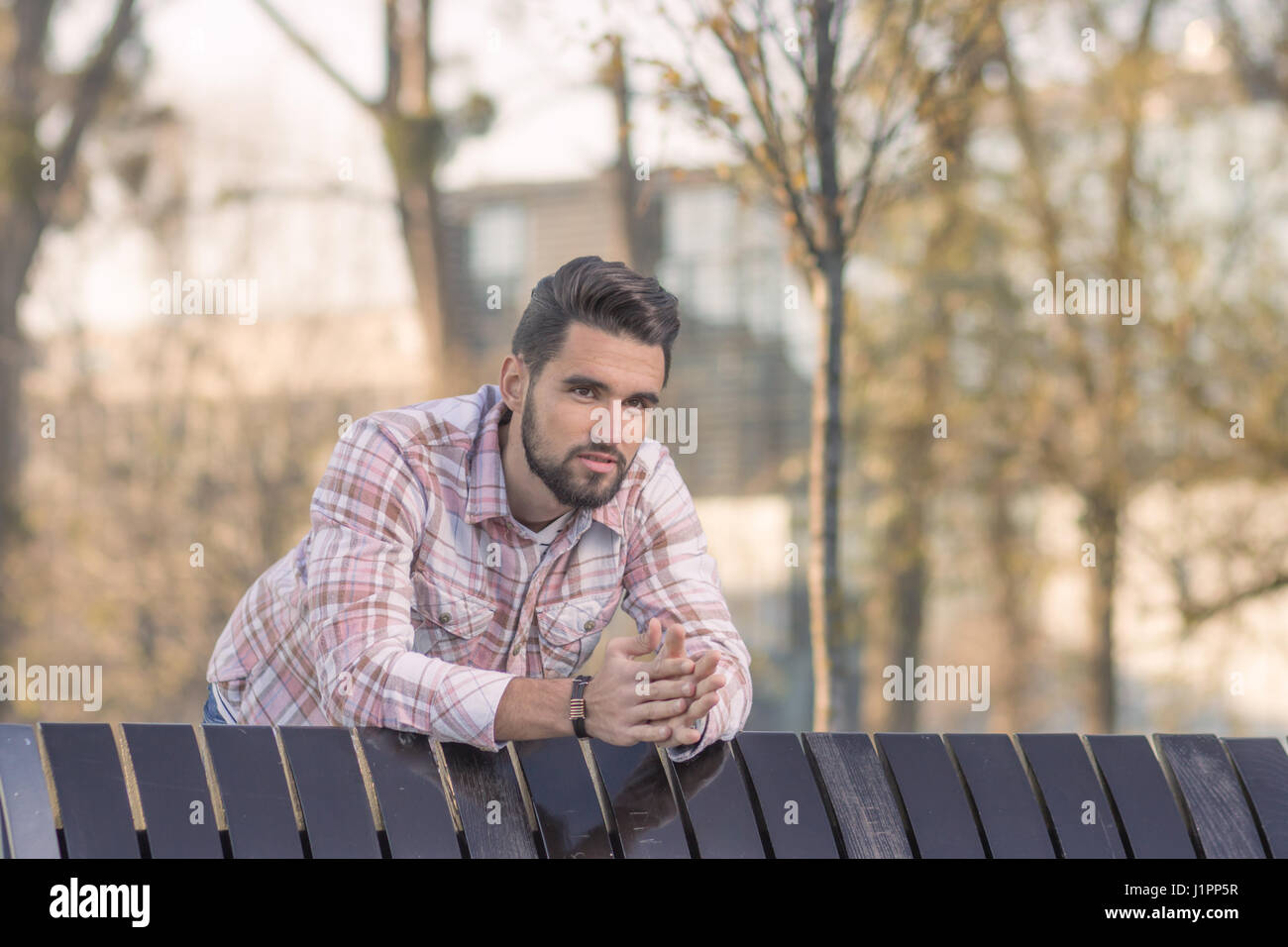 Young adult man leaning on bench, outdoors head, face, wearing shirt ...