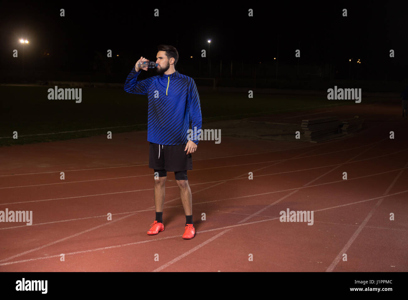 One young adult man, athlete, runner, drinking water. Dark night ...