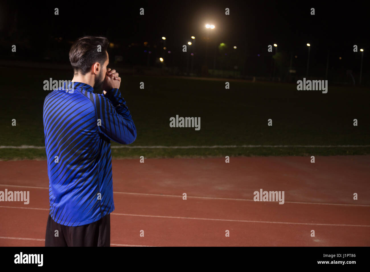 Rear view, athlete freezing, cold winter night stadium, football grass ...