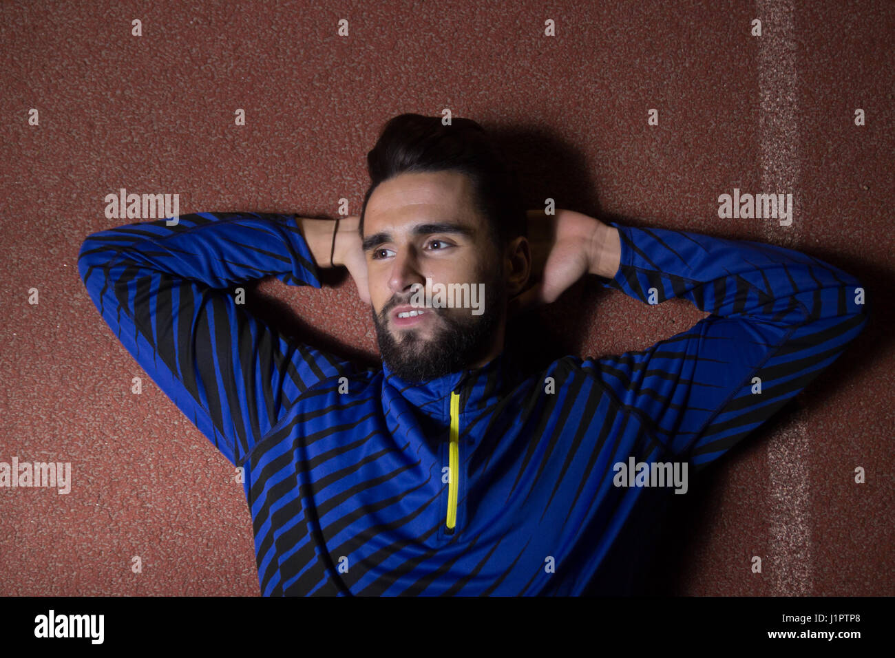 Close up, one young adult man, athlete laying relaxed, running track ...