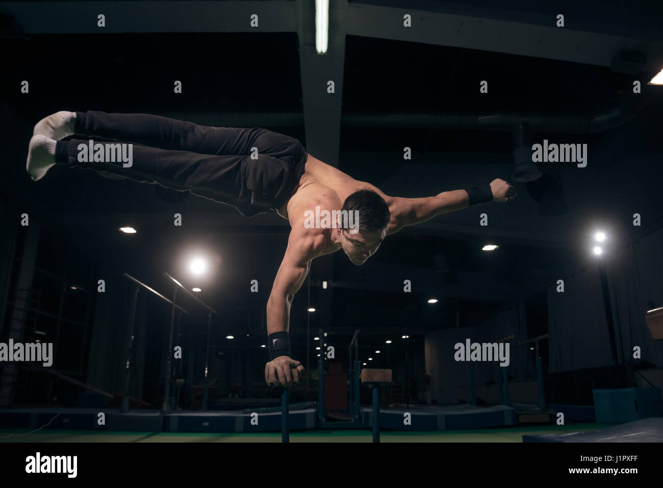 One young man, athlete, exercise one hand cartwheel. Dark large hall ...