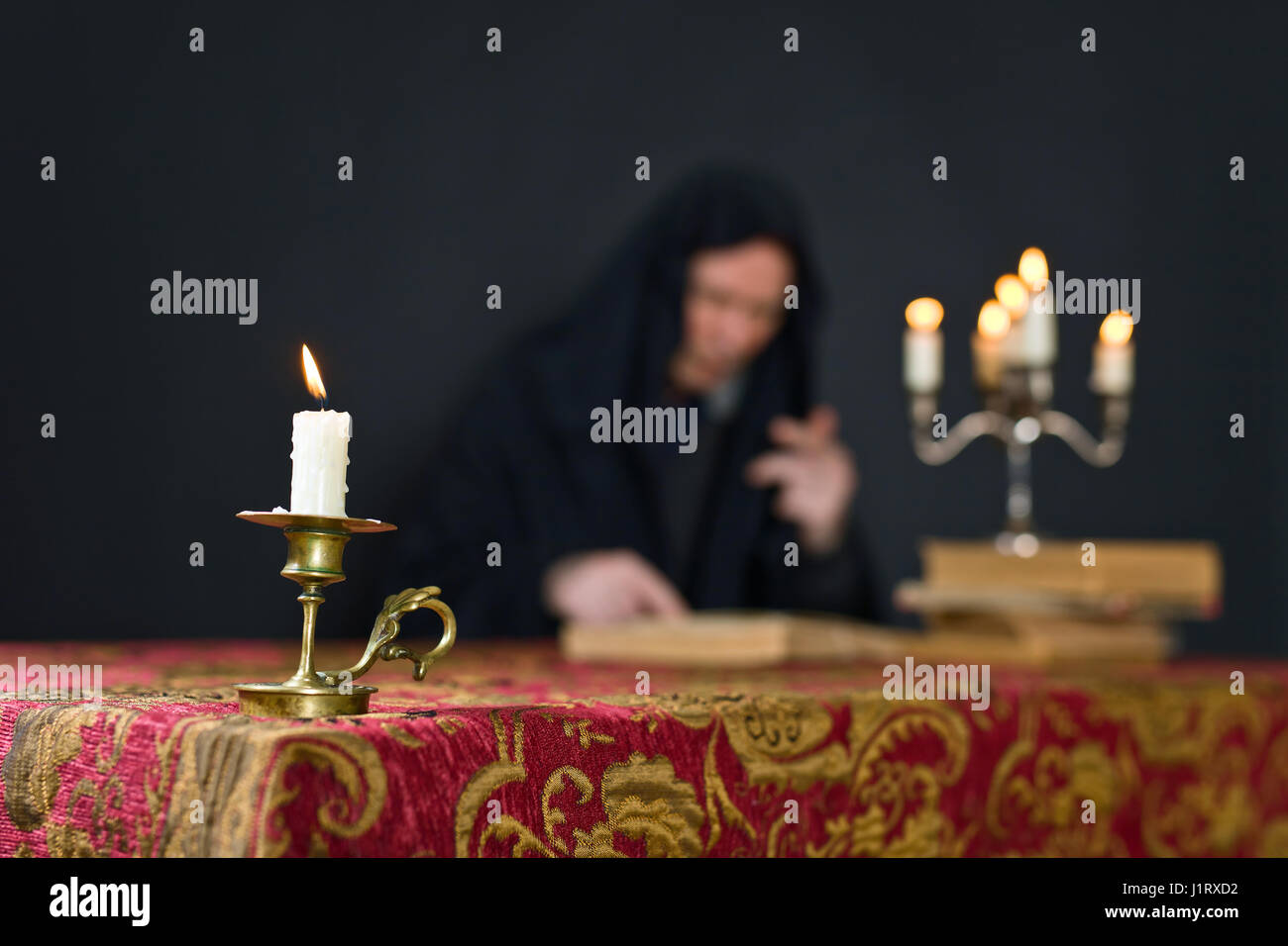 Burning candle in a small brass candlestick . A monk in a black robe ...