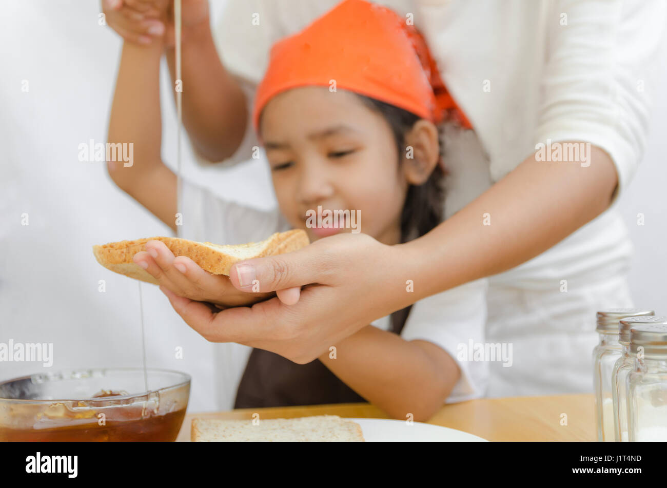 Asian little girl hold the bread and honey dipper stick with mother ...