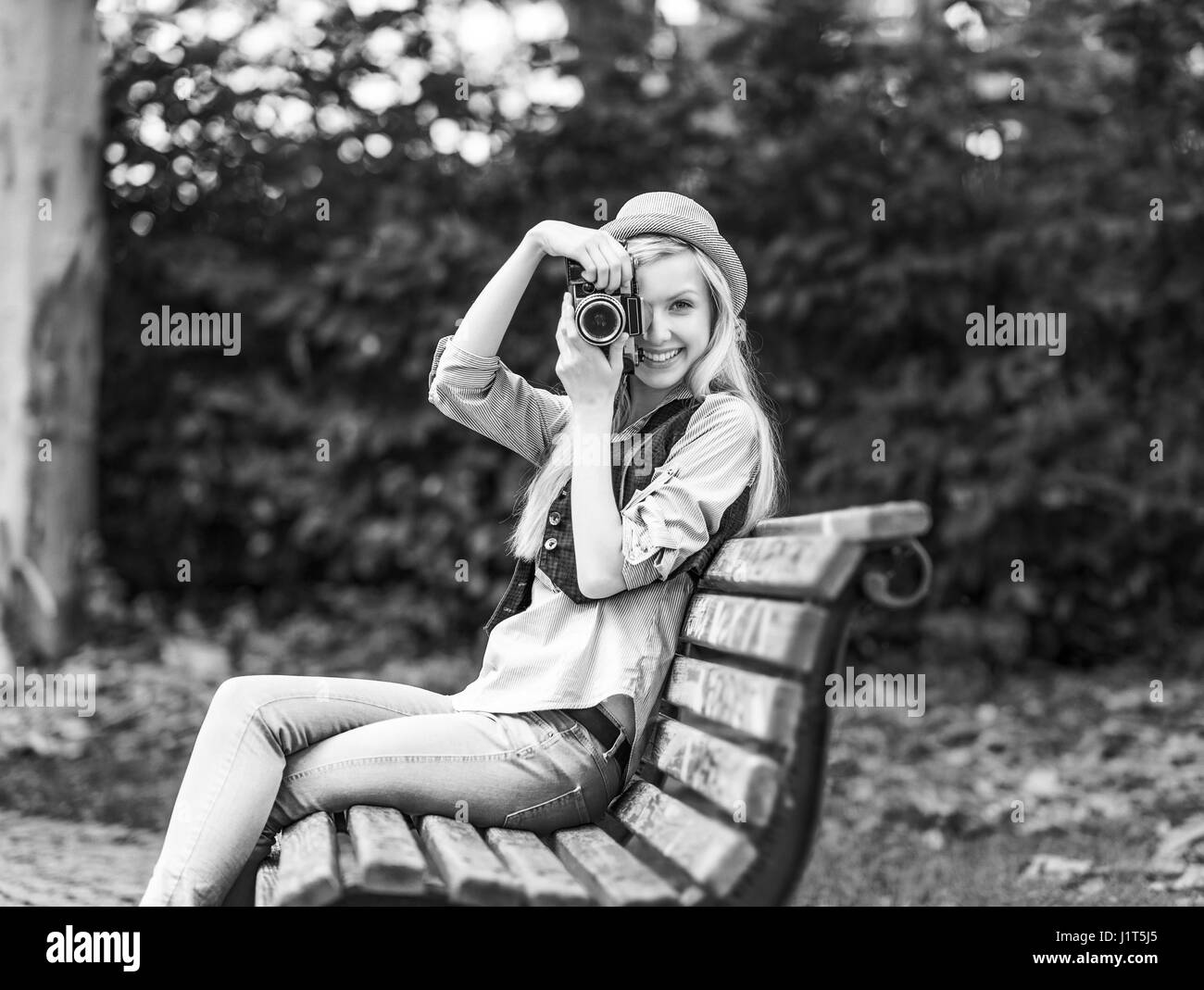 Young hipster taking photo with retro photo camera sitting on bench in ...