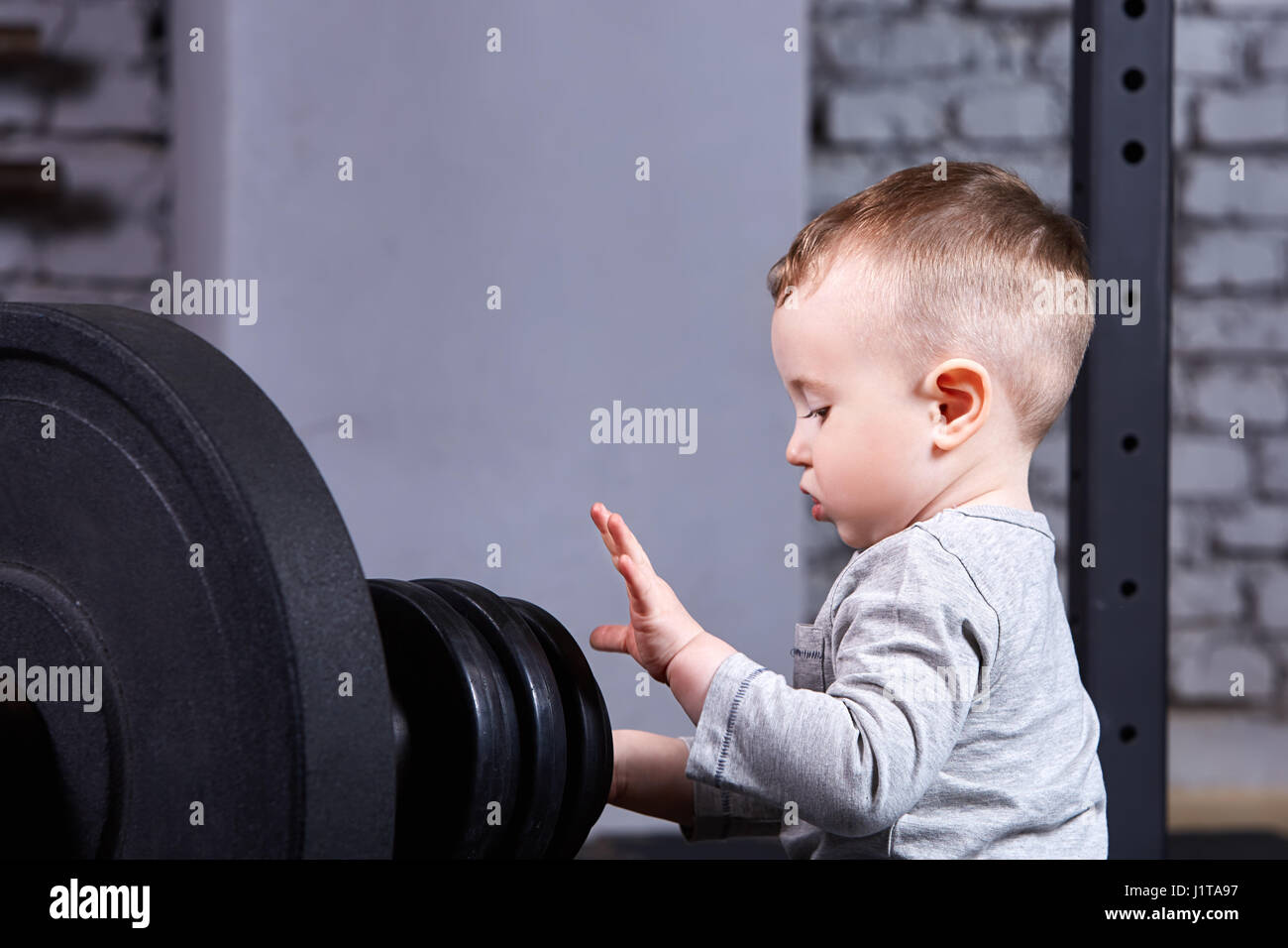 Close-up photo of little boy with barbell against brick wall in the ...