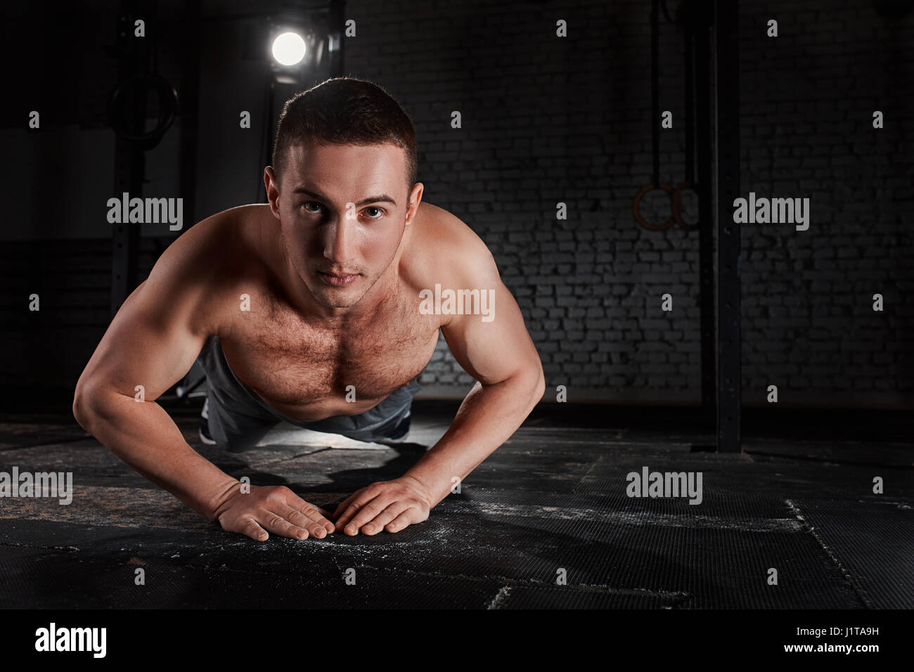 Young muscular man in the sportwear doing a pushups against brick wall ...