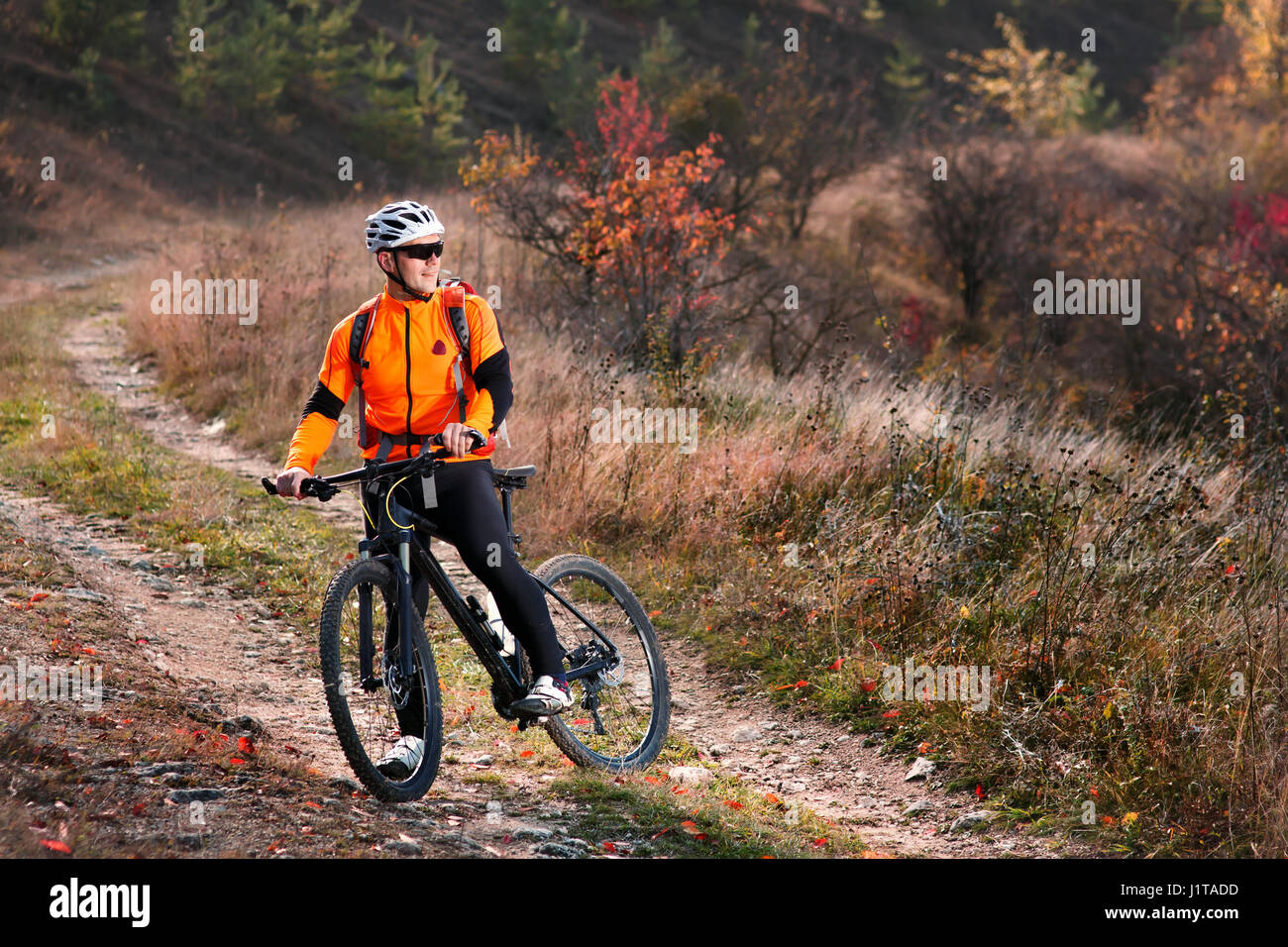Cyclist in the orange jacket riding a bike on countryside road at the ...