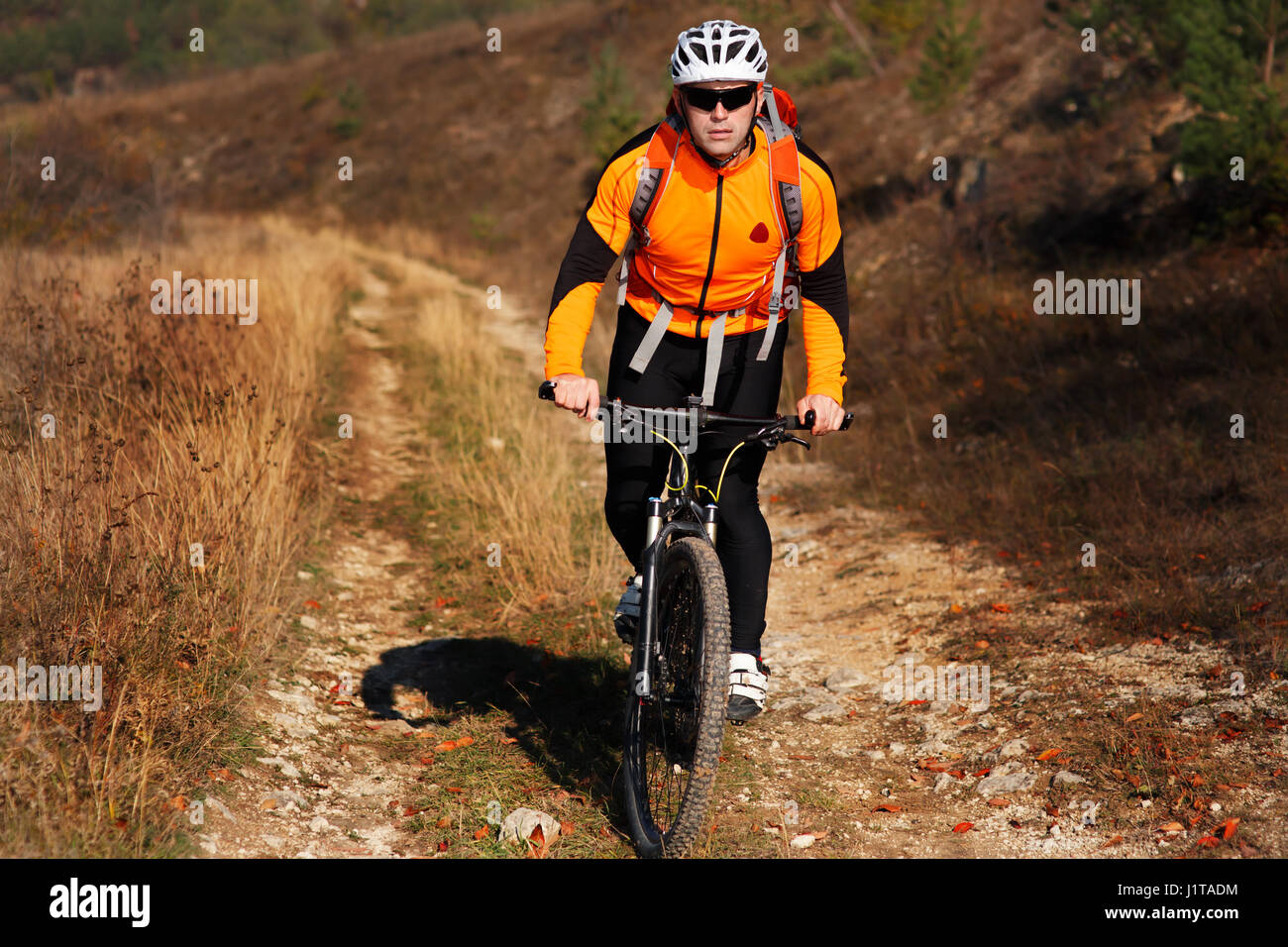 Cyclist in the orange jacket riding a bike on countryside road at the ...