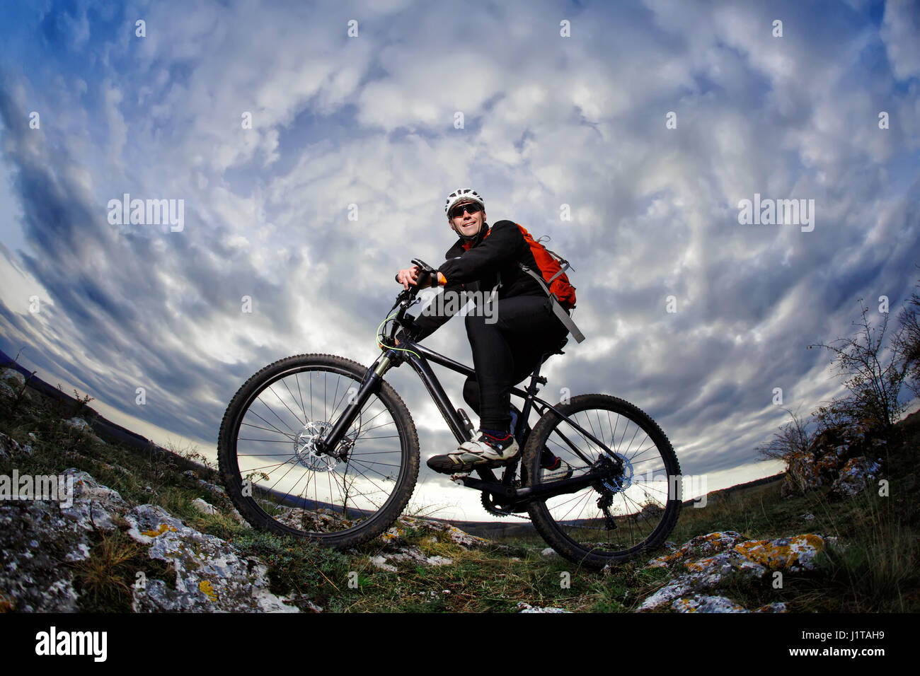 Cyclist in the black sportwear riding the bike on the rock at evening ...