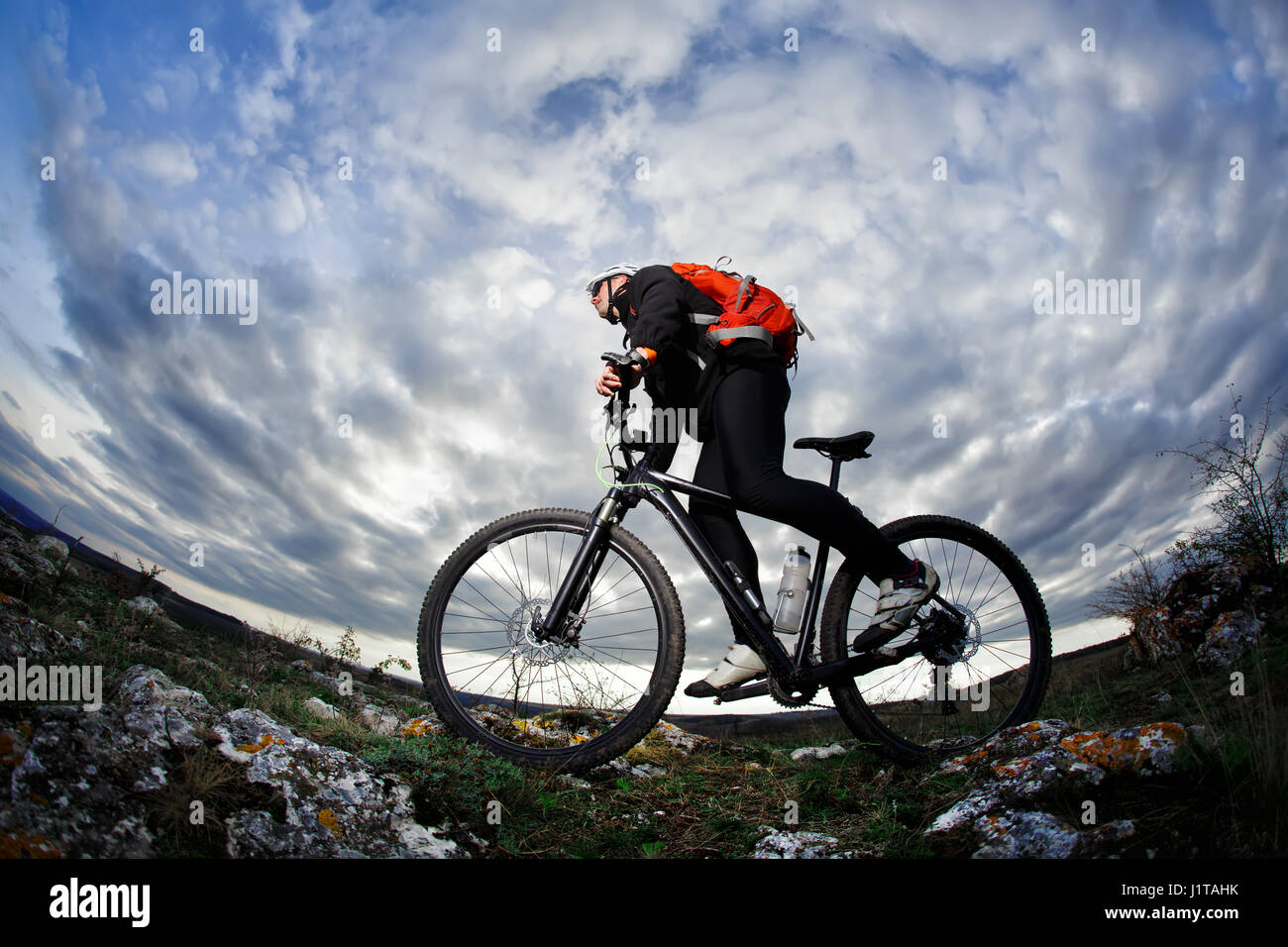 Cyclist in the black sportwear riding the bike on the rock at evening ...