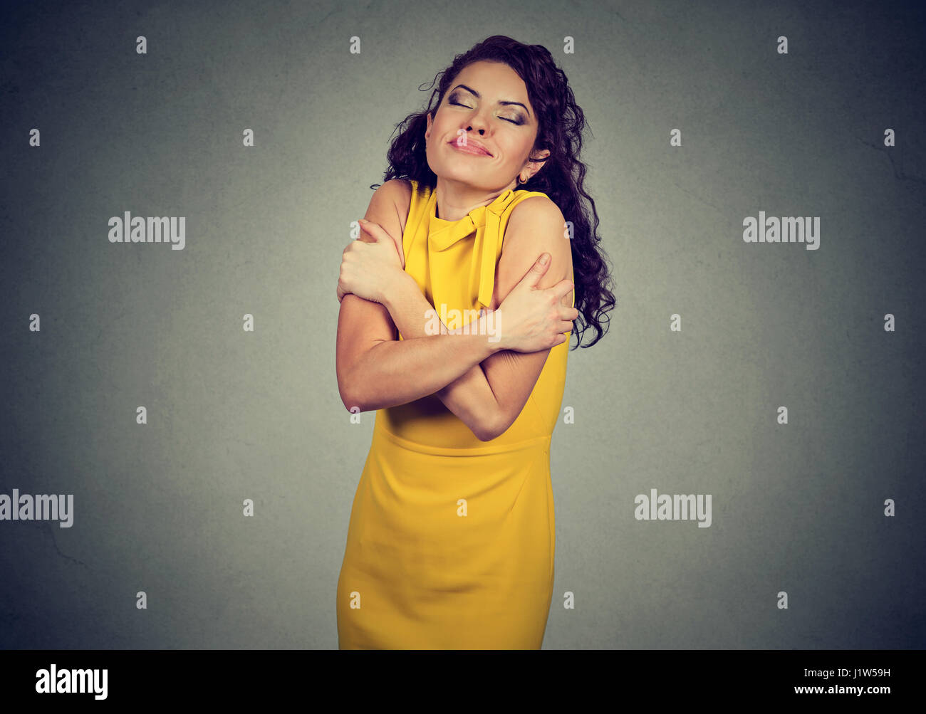 Smiling woman holding hugging herself isolated gray wall background ...