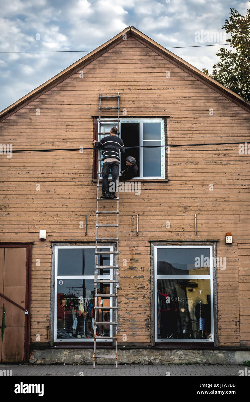 Man on ladder repairing old wooden house with the coworker looking at ...