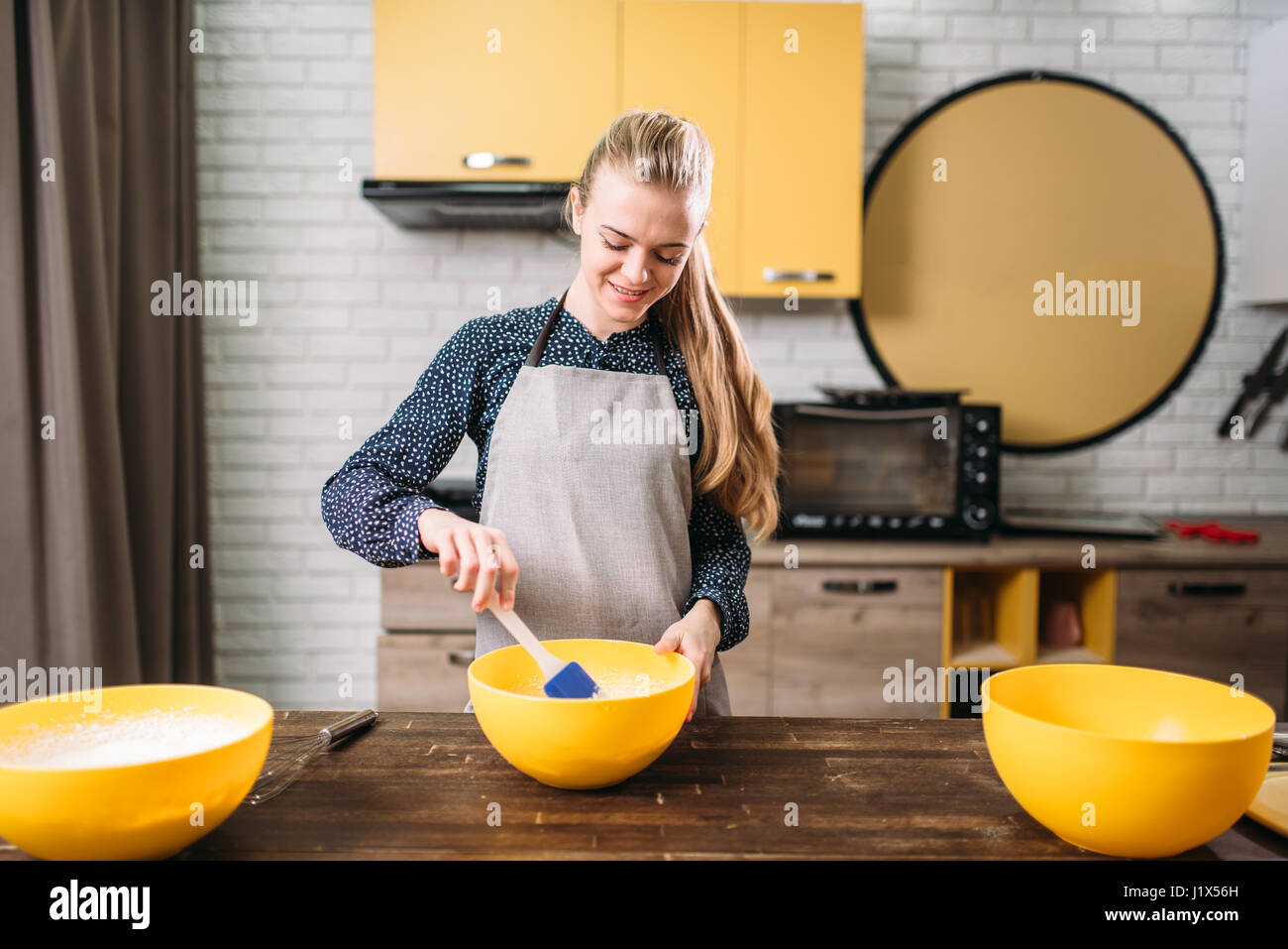 Young woman in apron stir the dough in a bowl on wooden table. Sweet ...