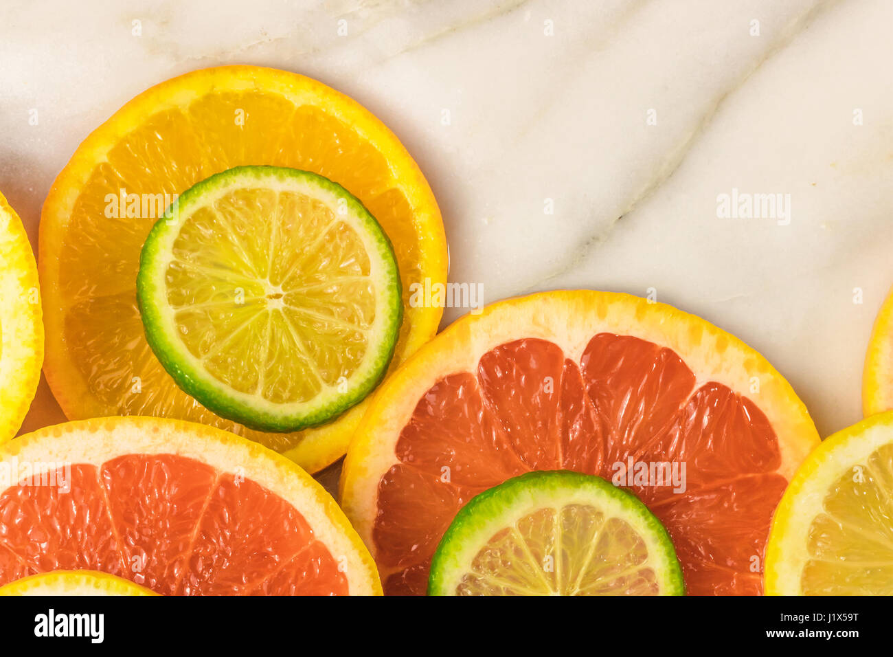 Vibrant juicy citrus fruits on a white marble texture with copy space ...