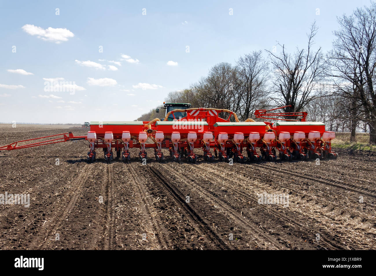Tractor with trailed planter working in field in a sunny spring day ...