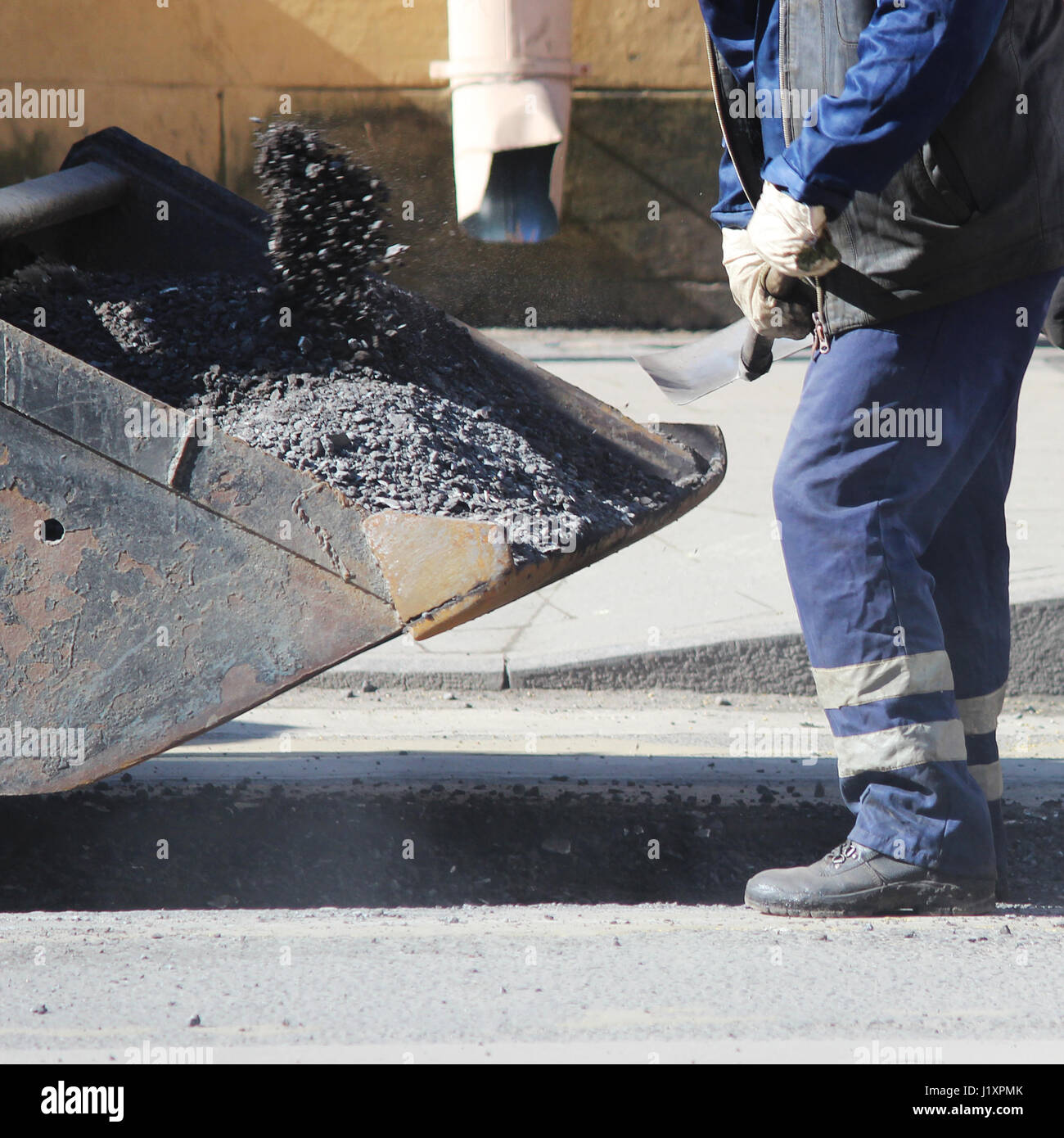 Road worker in overalls is poured with hot tar on the edge of the road ...