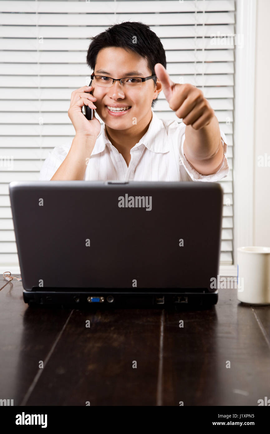 An asian entrepreneur giving a thumbs up while talking on the phone ...