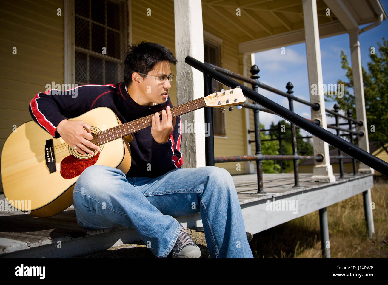 A young asian male playing guitar outside Stock Photo - Alamy
