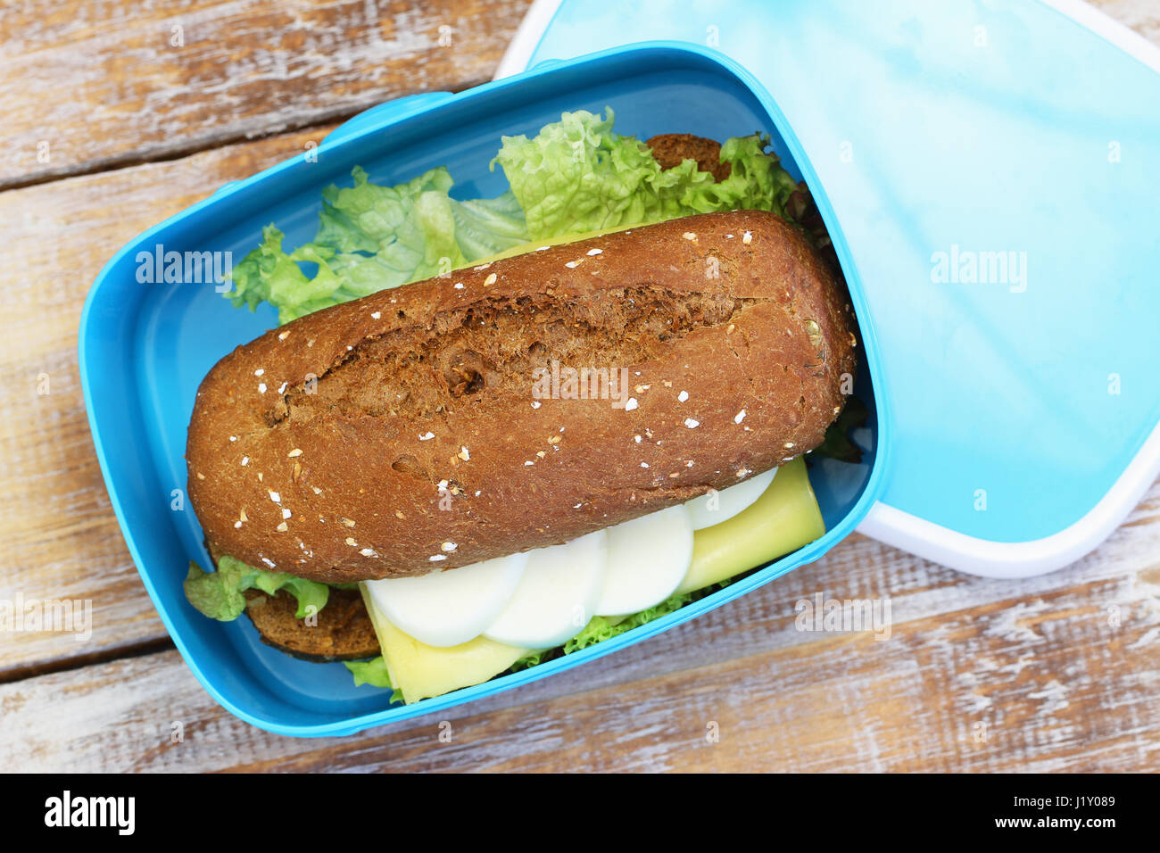 Lunch box containing brown roll with cheese and hard boiled egg and ...