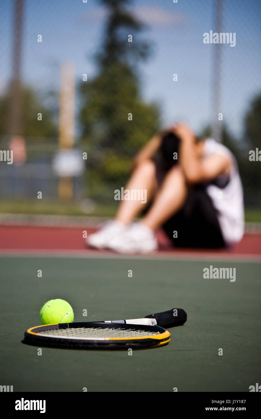 A sad male tennis player sitting down in disappointment after defeat ...