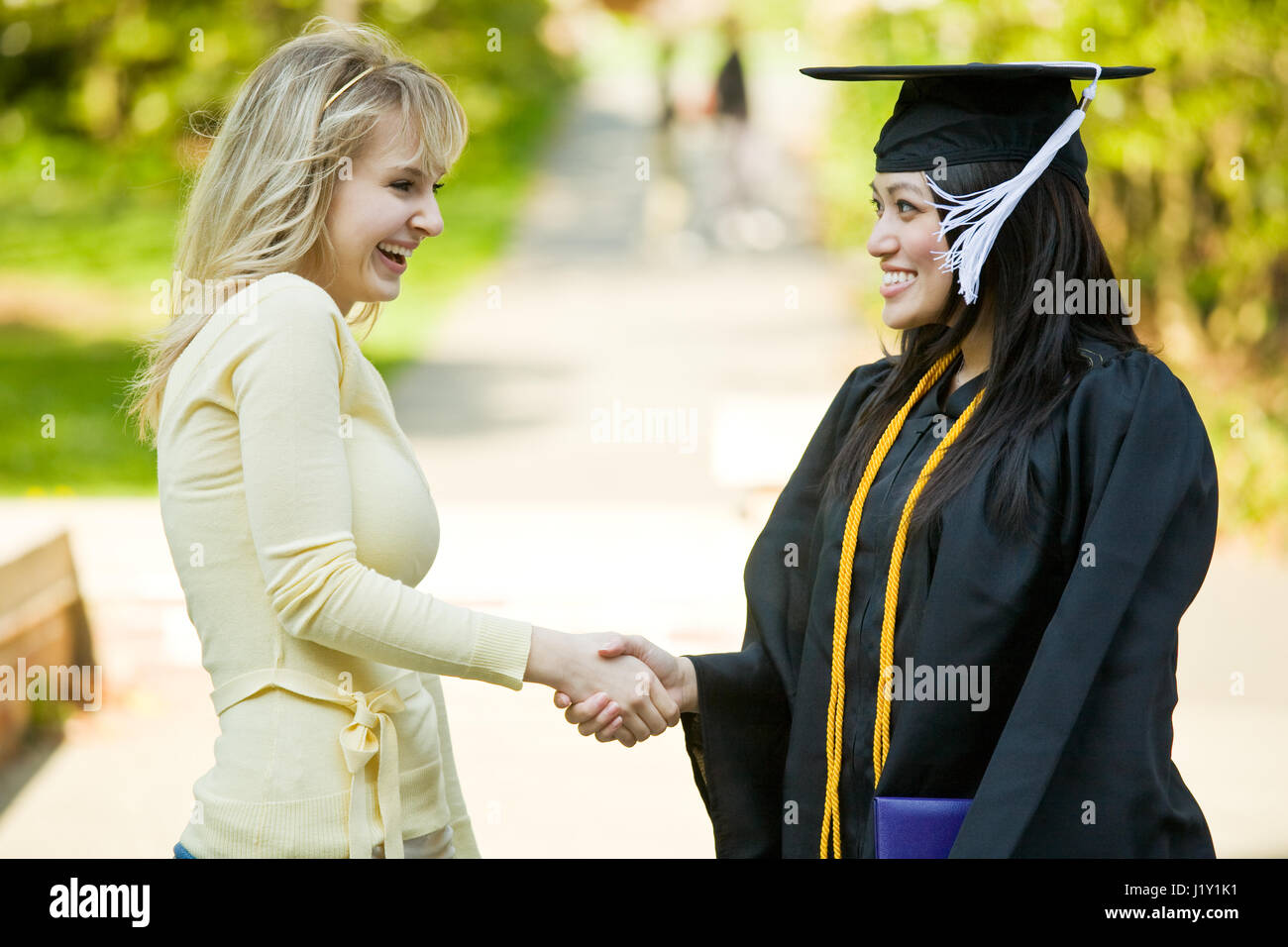 A happy beautiful graduation girl being congratulated by her friend ...