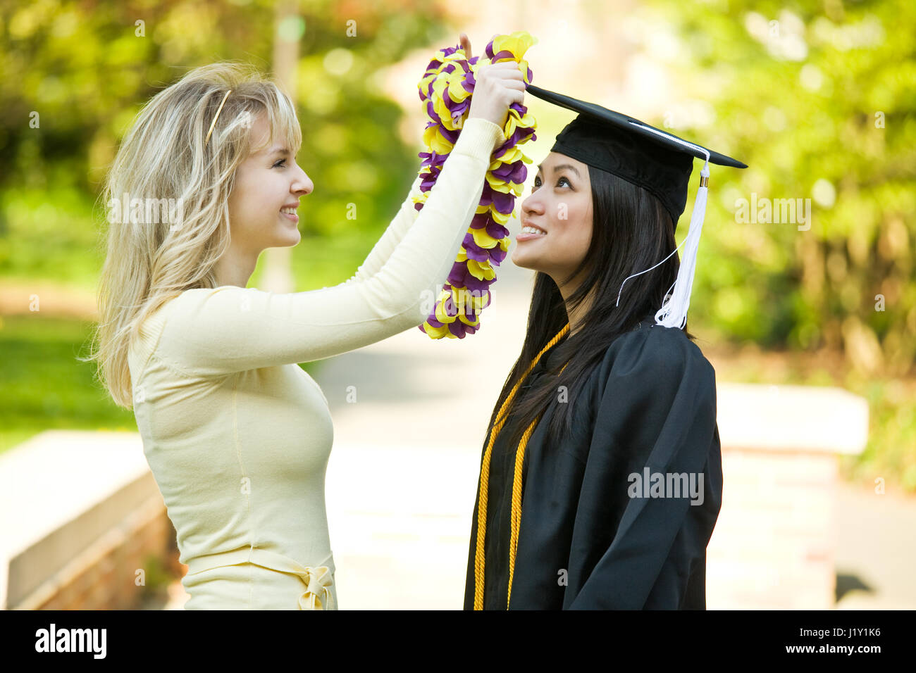 A happy beautiful graduation girl being congratulated by her friend ...