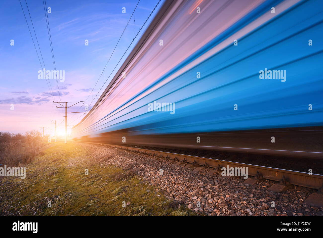 High speed blue passenger train in motion on railroad at sunset ...